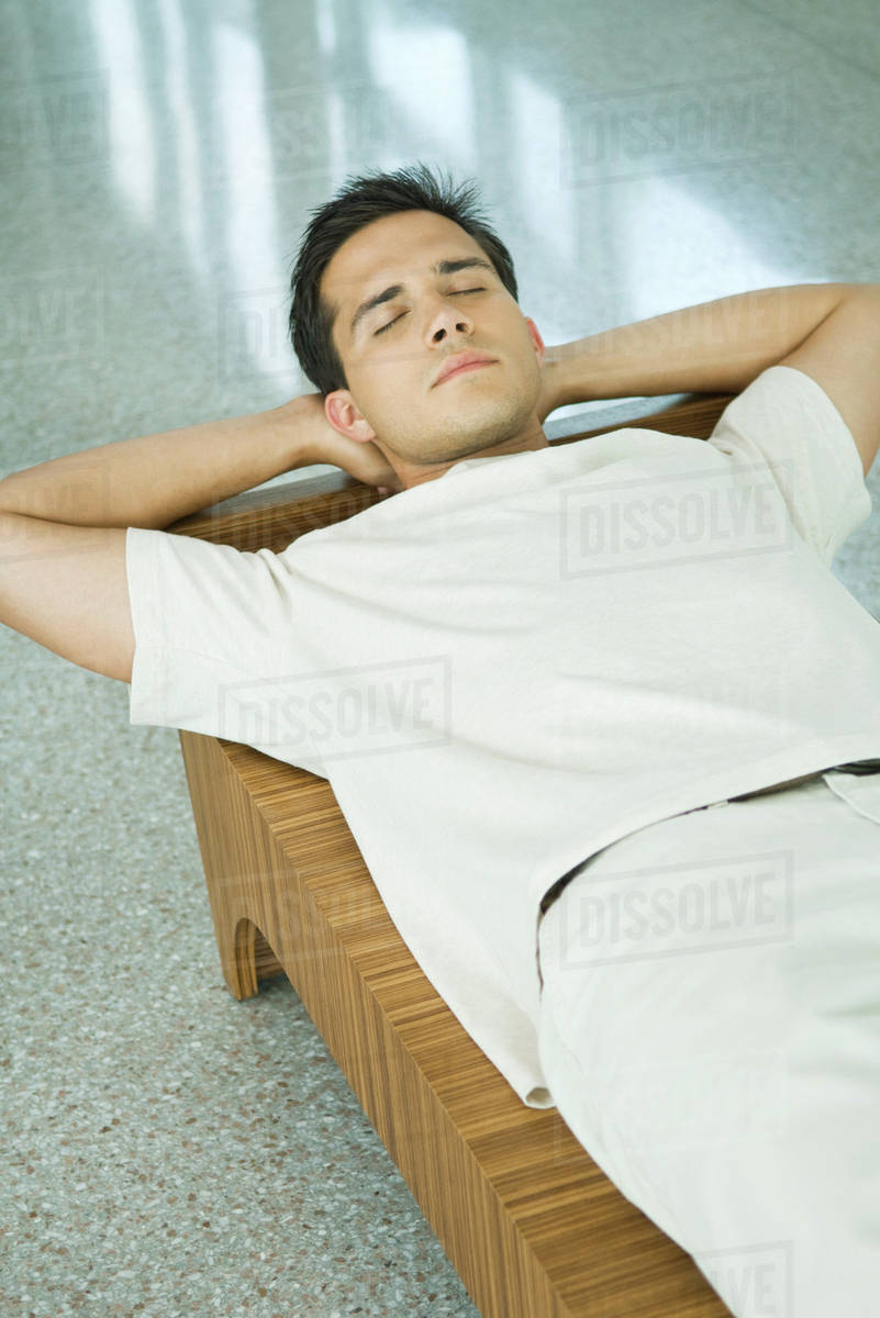 Young man lying on bench with hands behind head, eyes closed - Royalty ...
