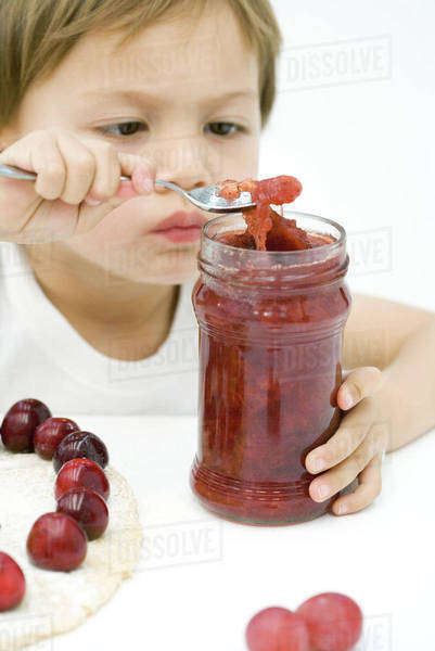 Little boy scooping jam out of jar with spoon, tart and cherries on ...