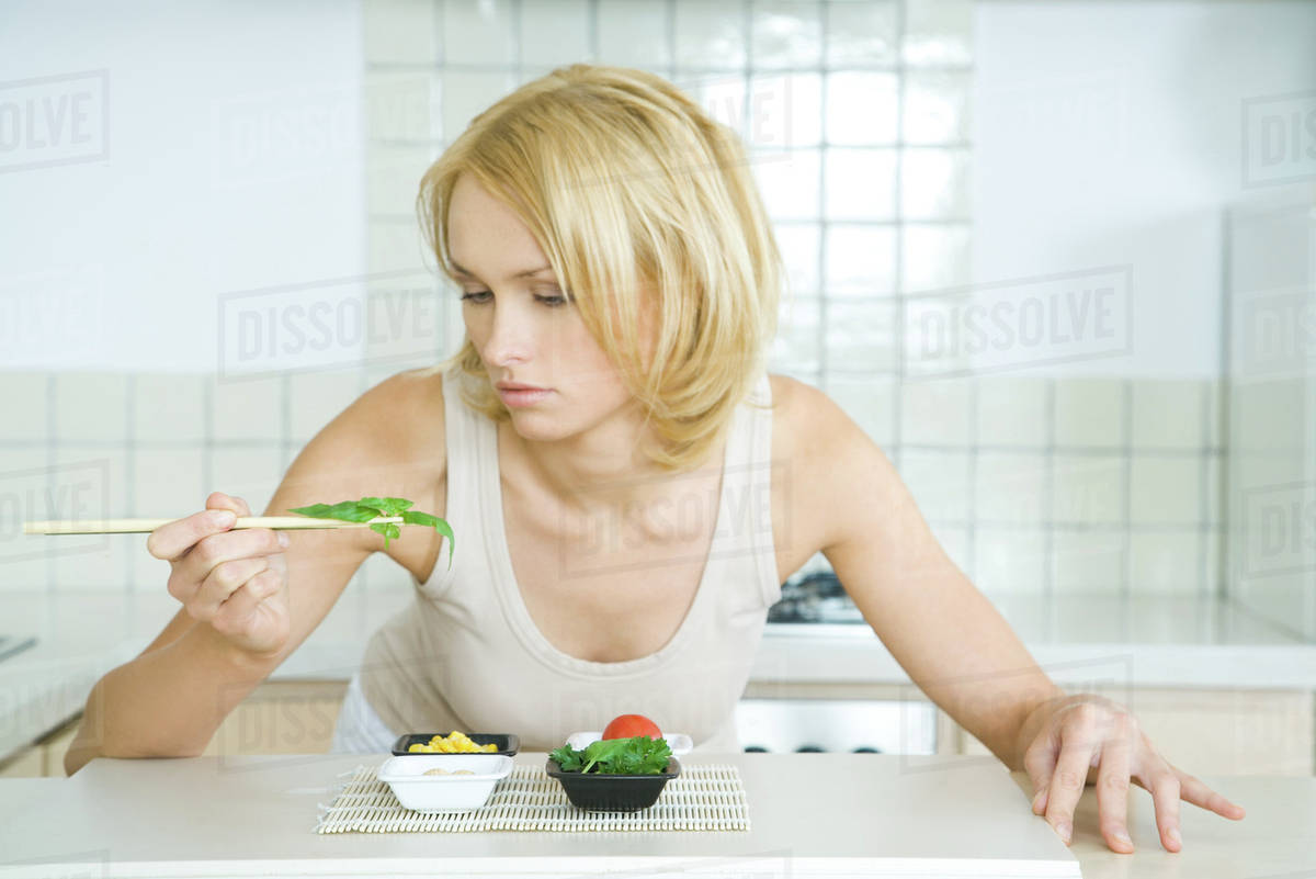 Young woman leaning over kitchen counter, picking up herbs with ...