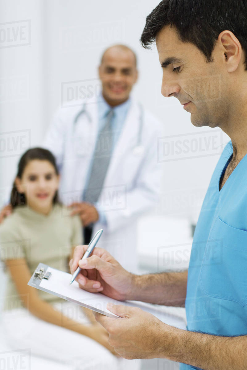 Male nurse writing on clipboard, young patient and doctor in background ...