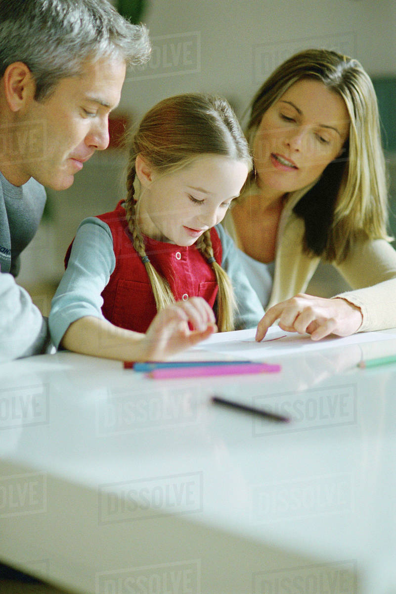Little girl doing homework with parents - Stock Photo - Dissolve