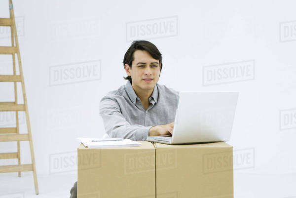 Man working on laptop computer, using cardboard boxes as makeshift desk ...