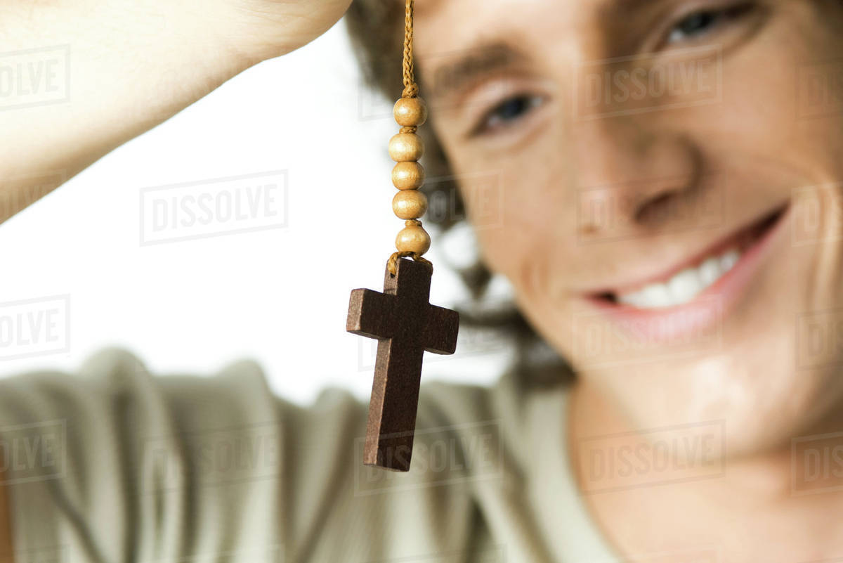 Young man looking at cross, smiling, close-up - Stock Photo - Dissolve