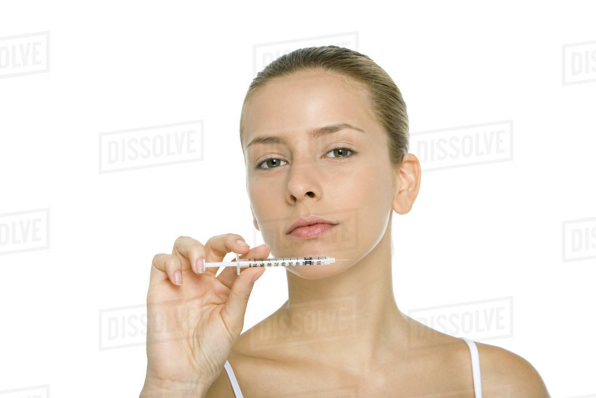 Woman holding up syringe, looking at camera - Stock Photo - Dissolve