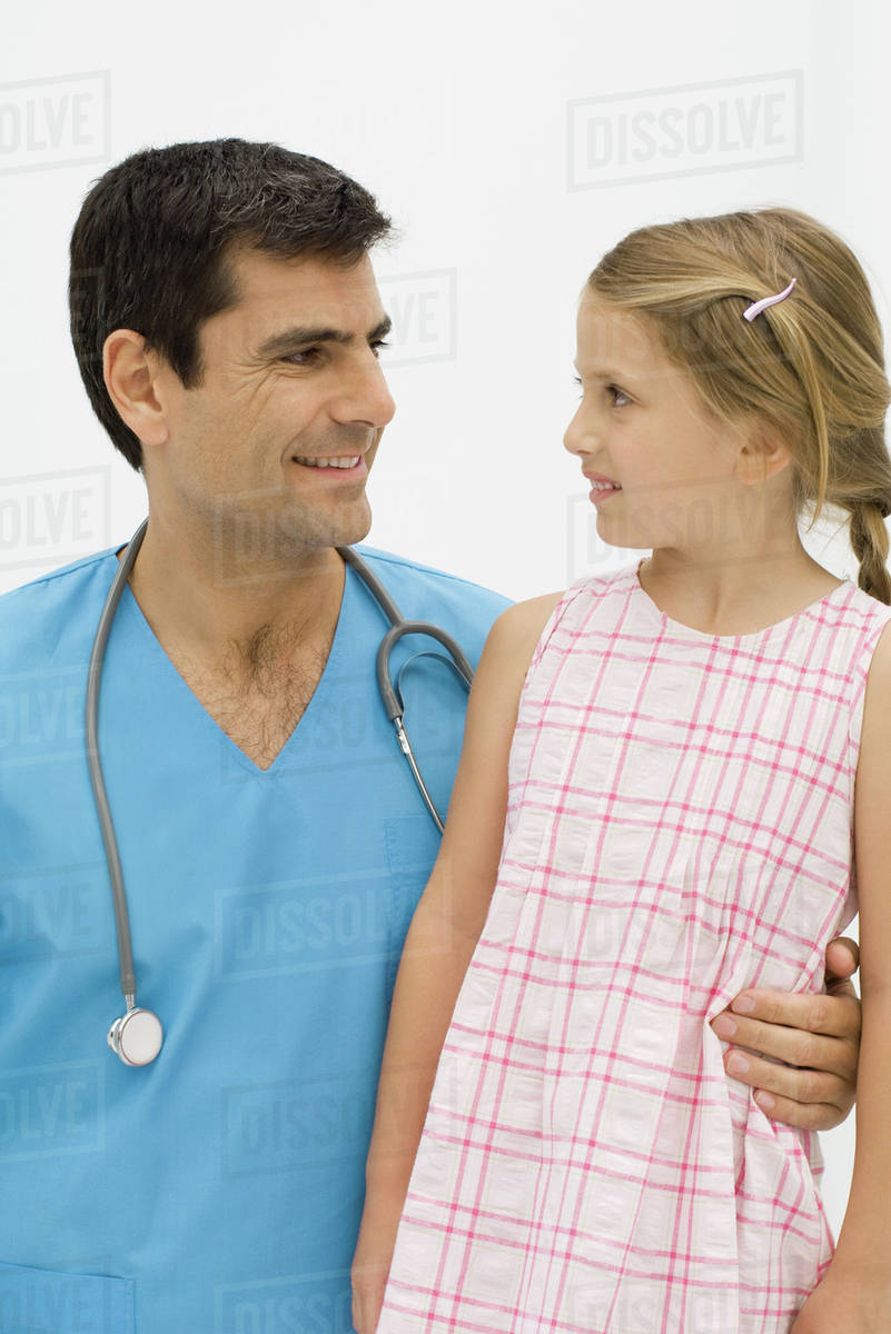 Doctor with arm around little girl's waist, both smiling at one another ...