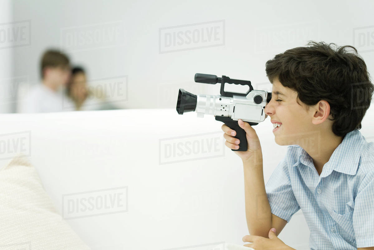 Boy looking through video camera, couple in background, side view ...
