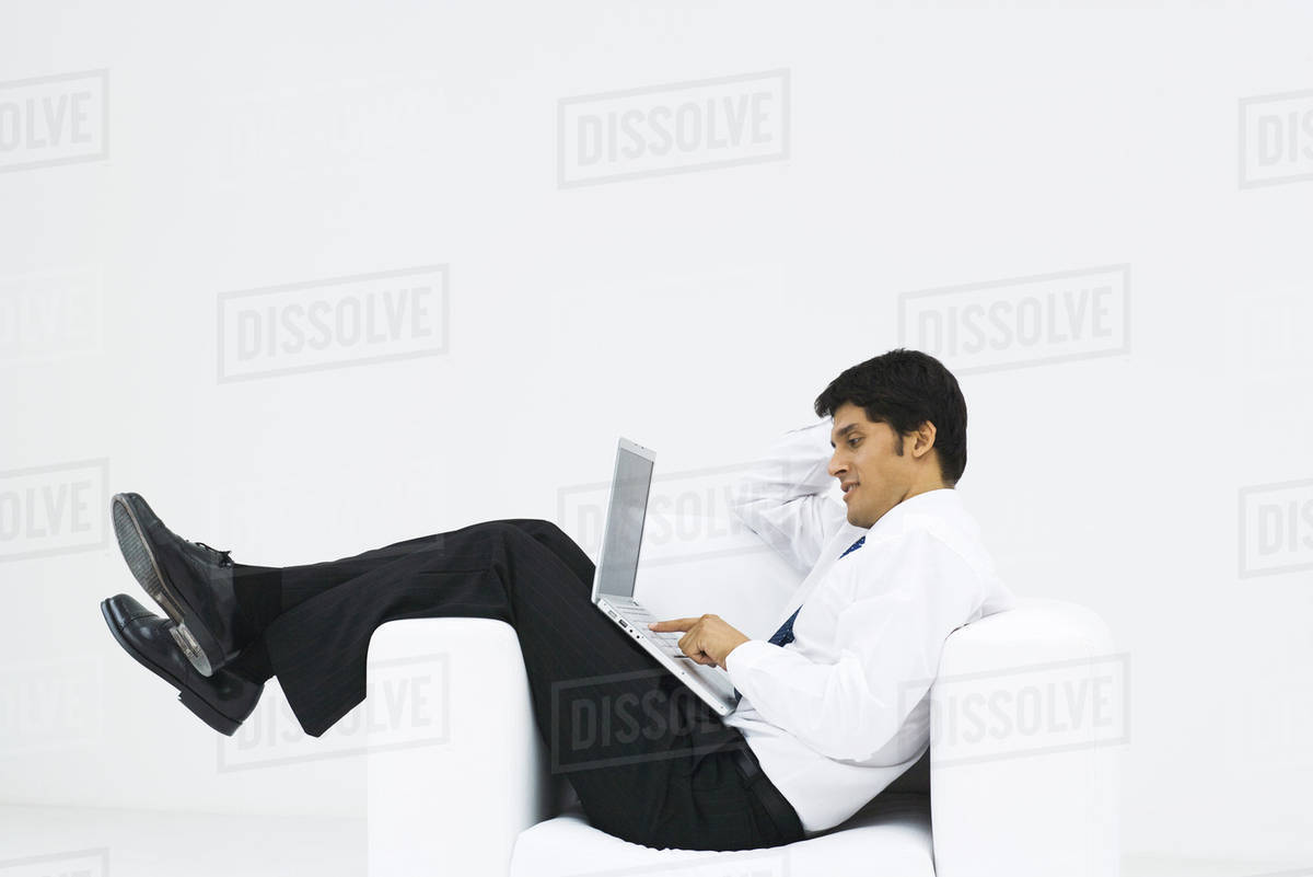Man slouching in armchair, using laptop, side view - Royalty-free Stock ...