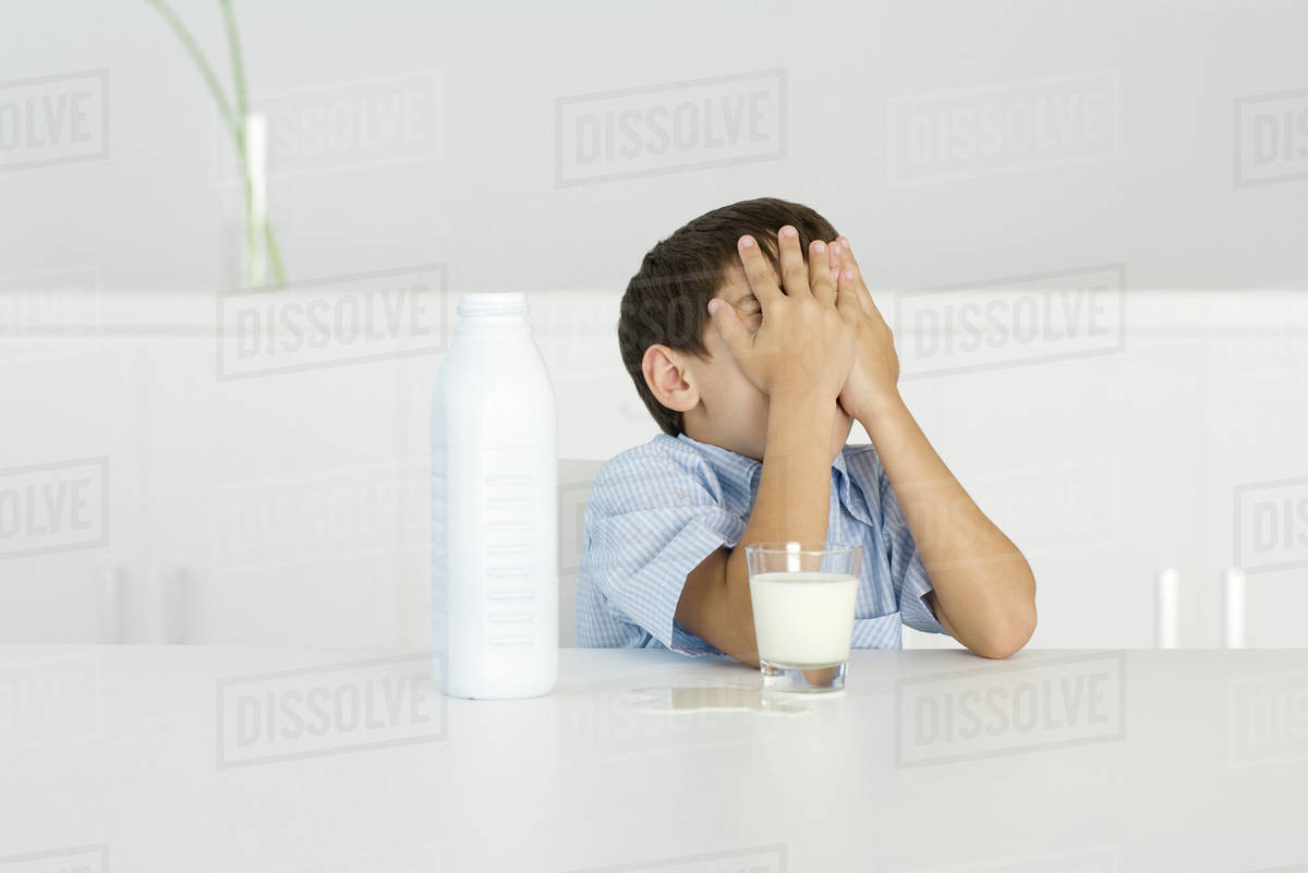 Boy with spilled milk, covering face with hands - Stock Photo - Dissolve