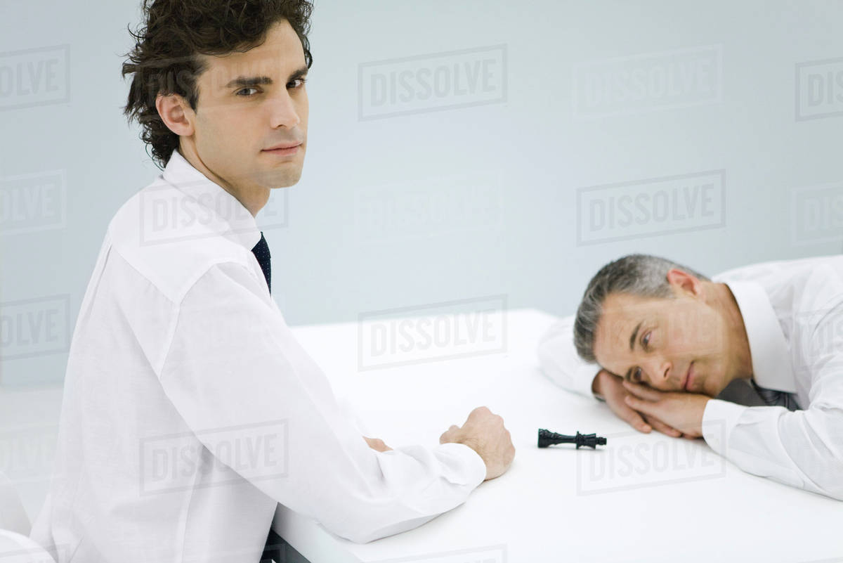 Young businessman sitting across table from defeated older businessman ...