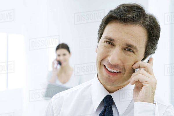Professional man using cell phone, smiling at camera, woman on phone in ...