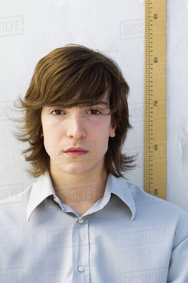 Young man standing in front of ruler, looking at camera - Stock Photo ...