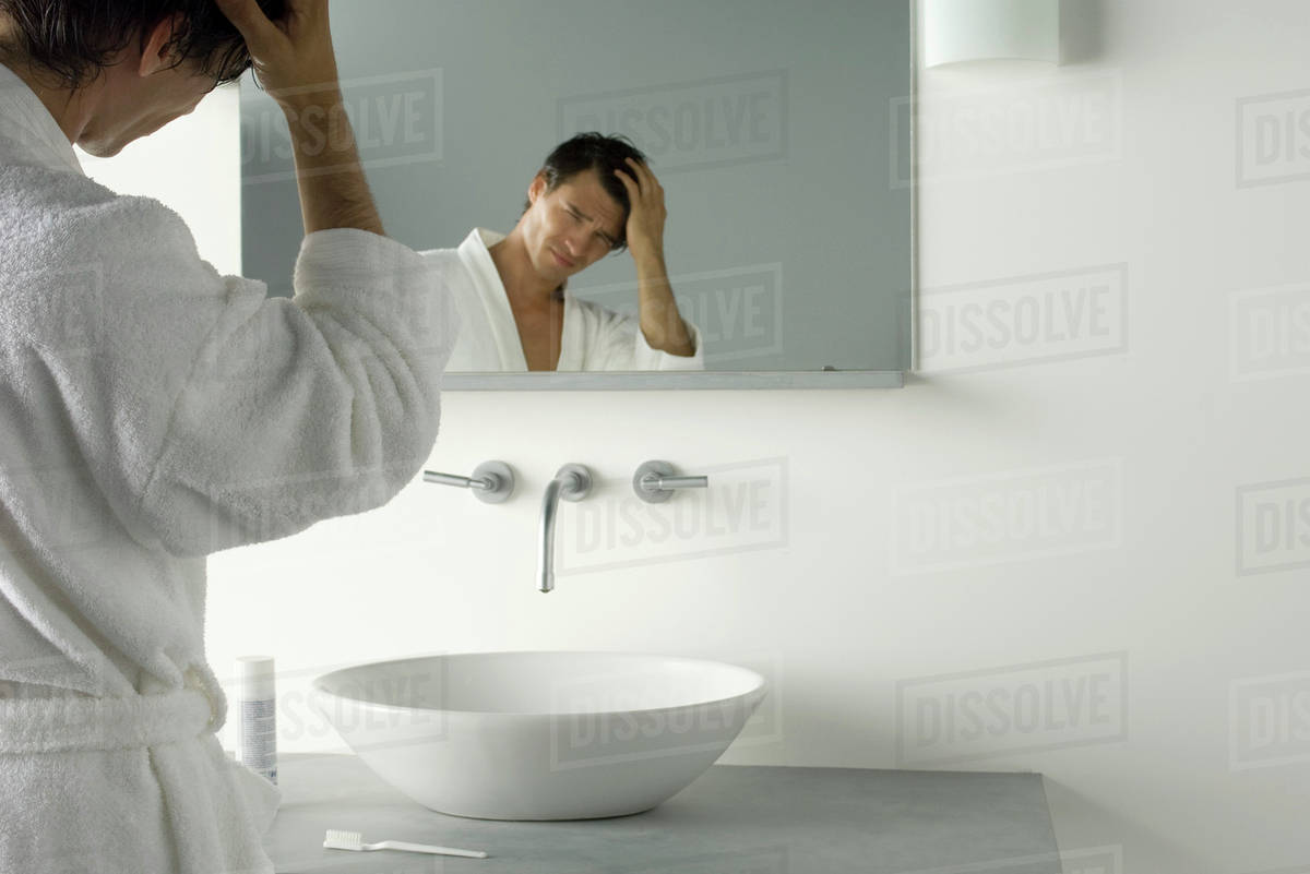 Man holding head, frowning at himself in mirror - Royalty-free Stock ...