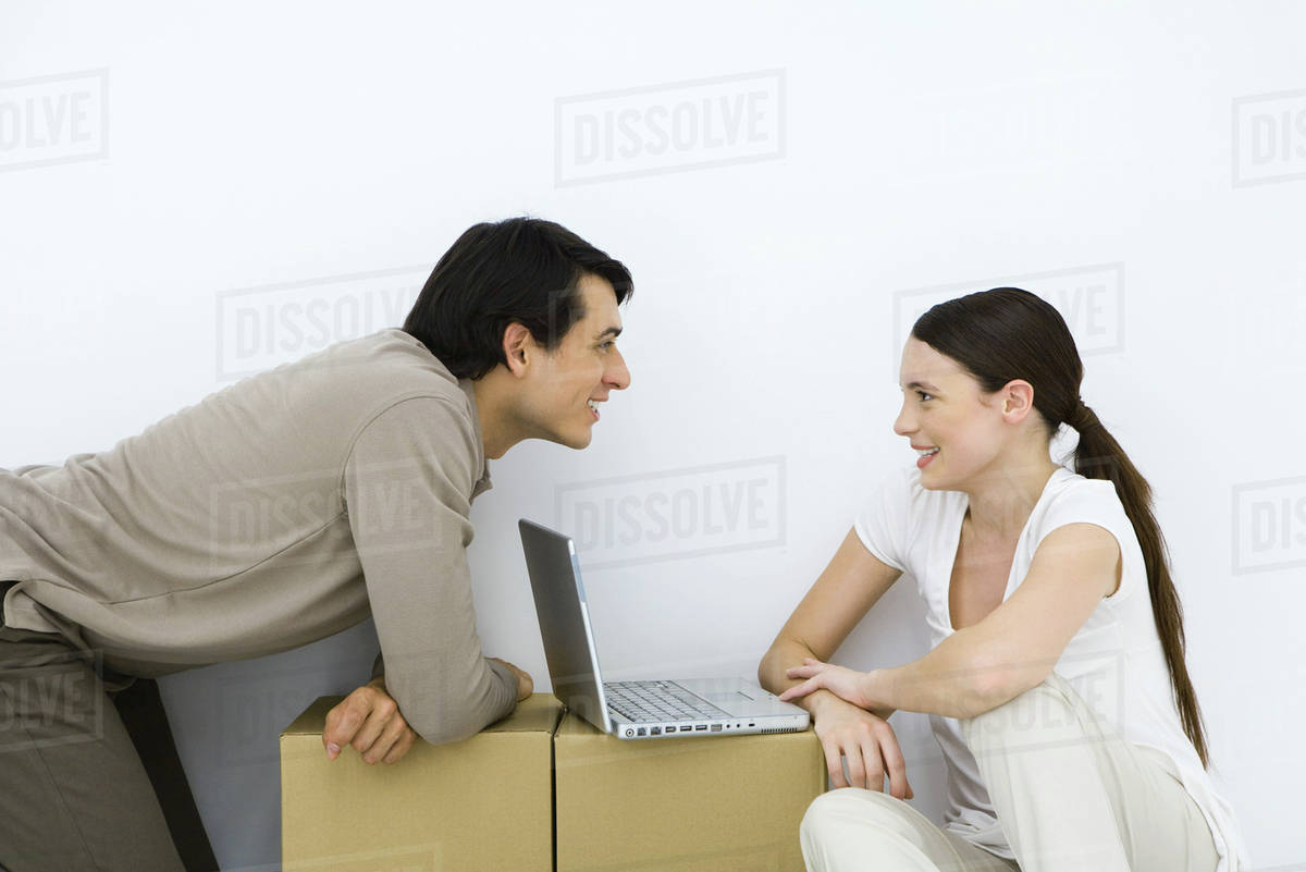 Couple sitting at makeshift desk with laptop computer between them ...