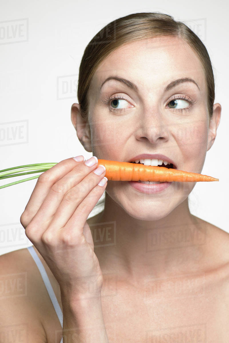 Young woman biting into carrot - Royalty-free Stock Photo | Dissolve