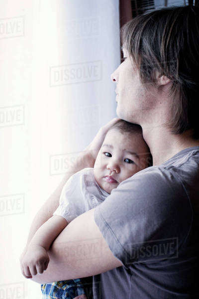 Father holding baby, looking out window - Stock Photo - Dissolve
