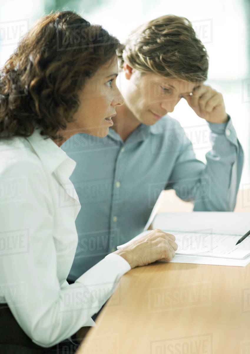 Mature couple sitting at table, man looking down at document, woman ...
