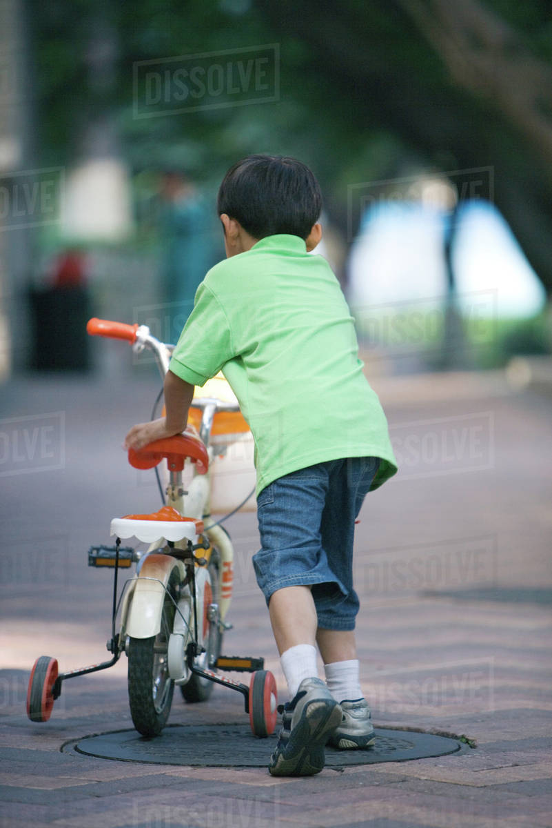 Boy walking with bicycle with training wheels, rear view - Royalty-free ...