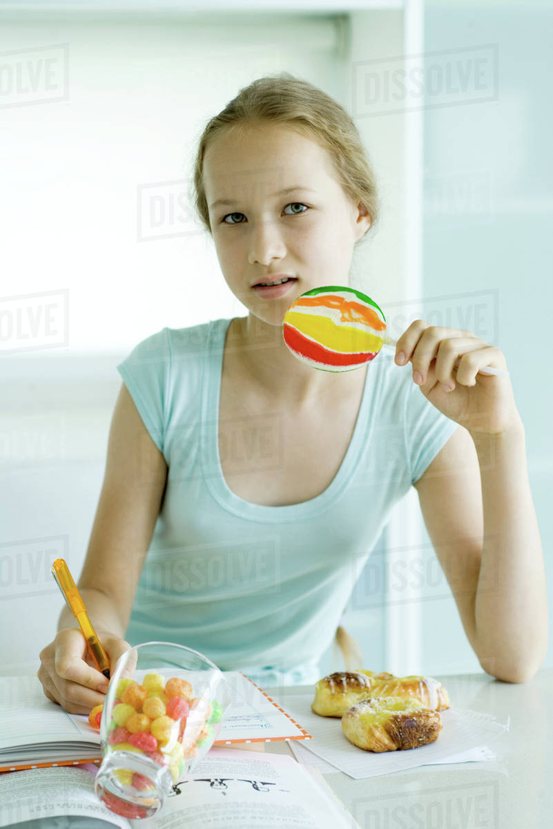 Girl eating sweets and doing homework - Royalty-free Stock Photo | Dissolve