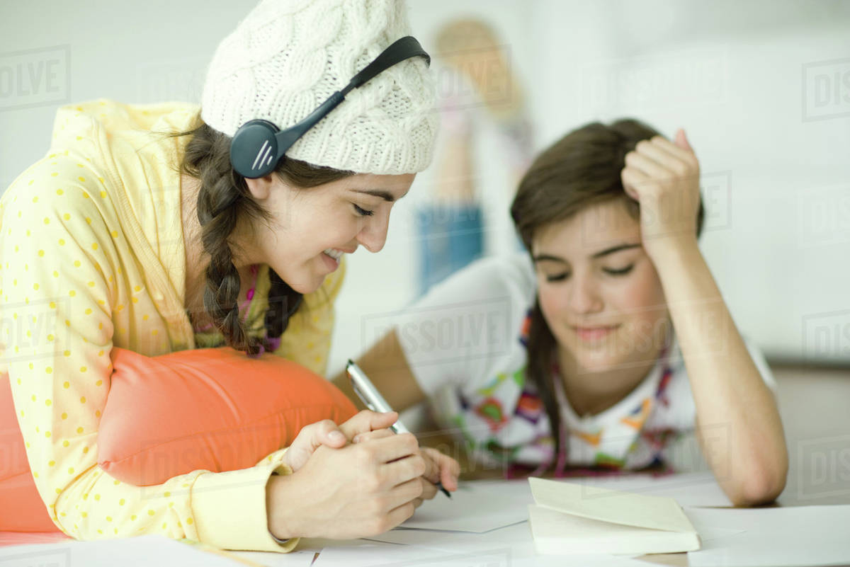 Two young female friends lying on floor, doing homework together ...