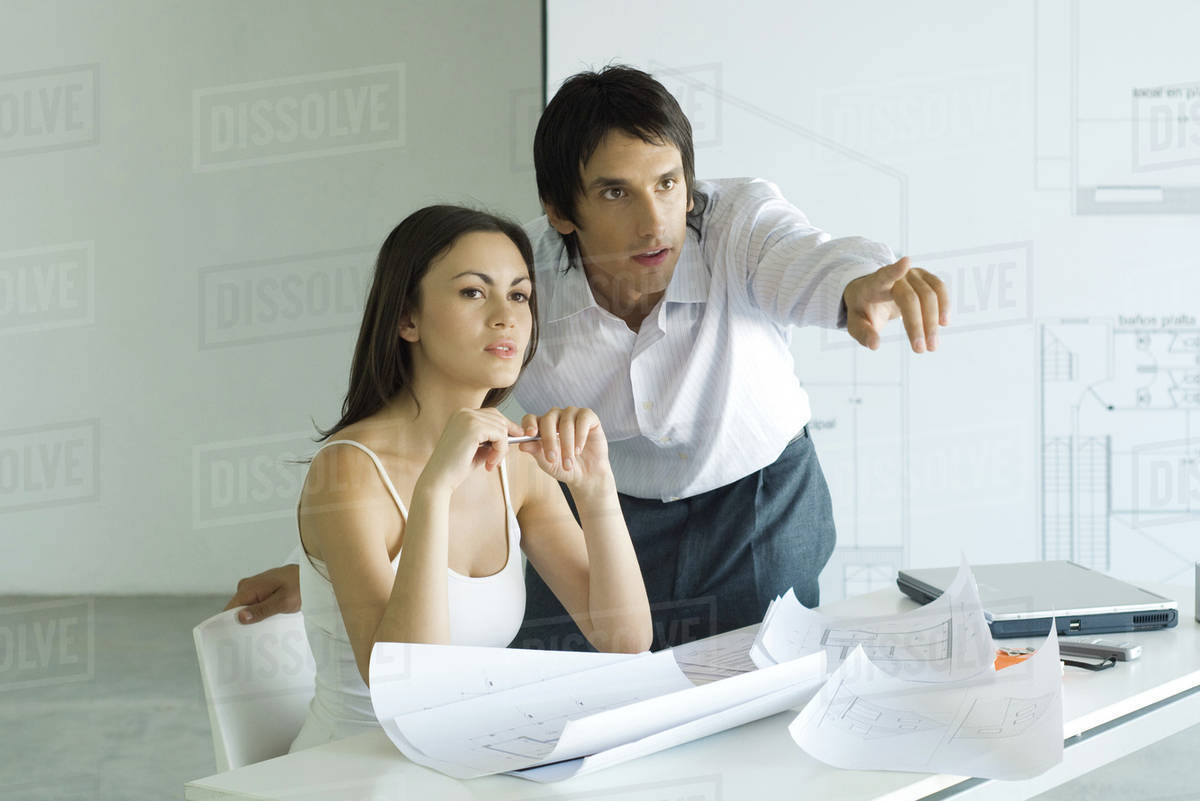 Couple next to table with blueprints, man leaning over woman's shoulder ...