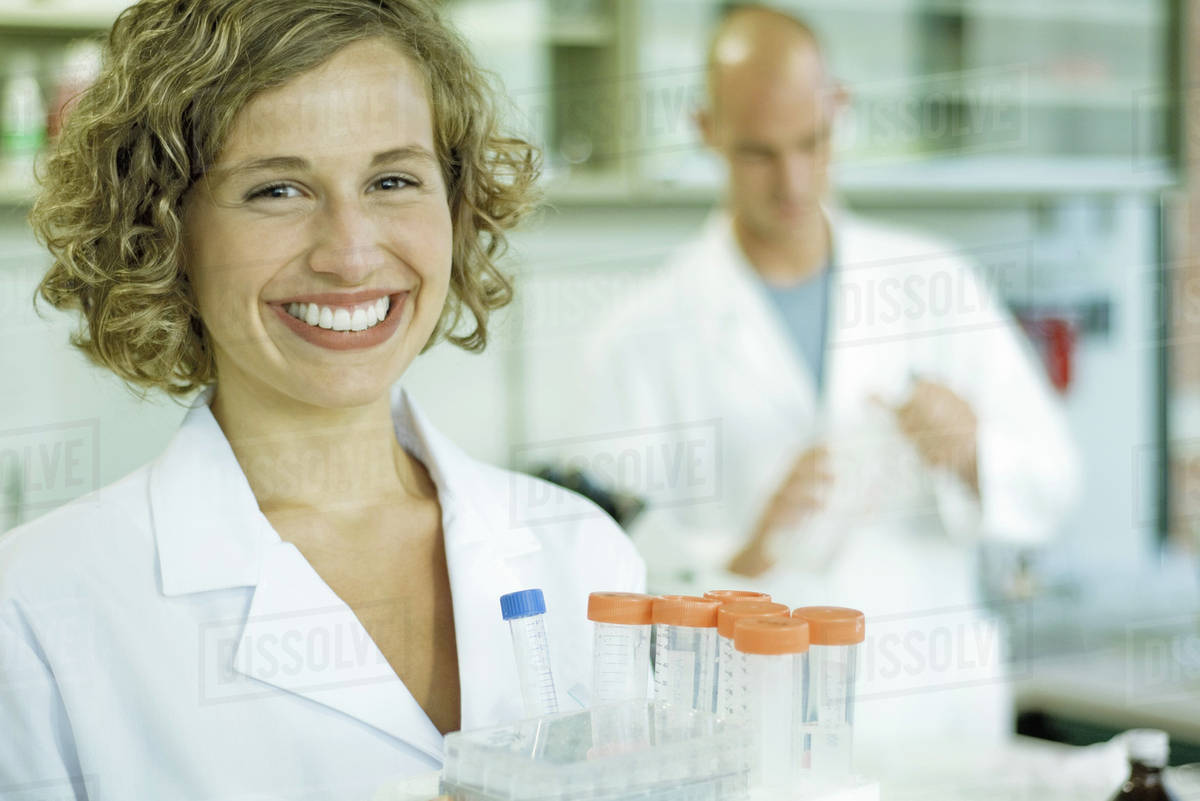 Female lab worker holding rack of empty test tubes, smiling at camera ...