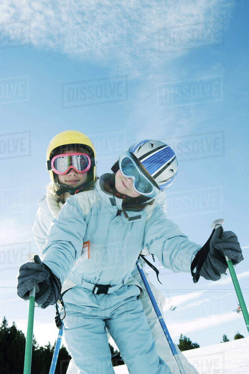 Two young skiers standing, one behind the other, both smiling at camera ...