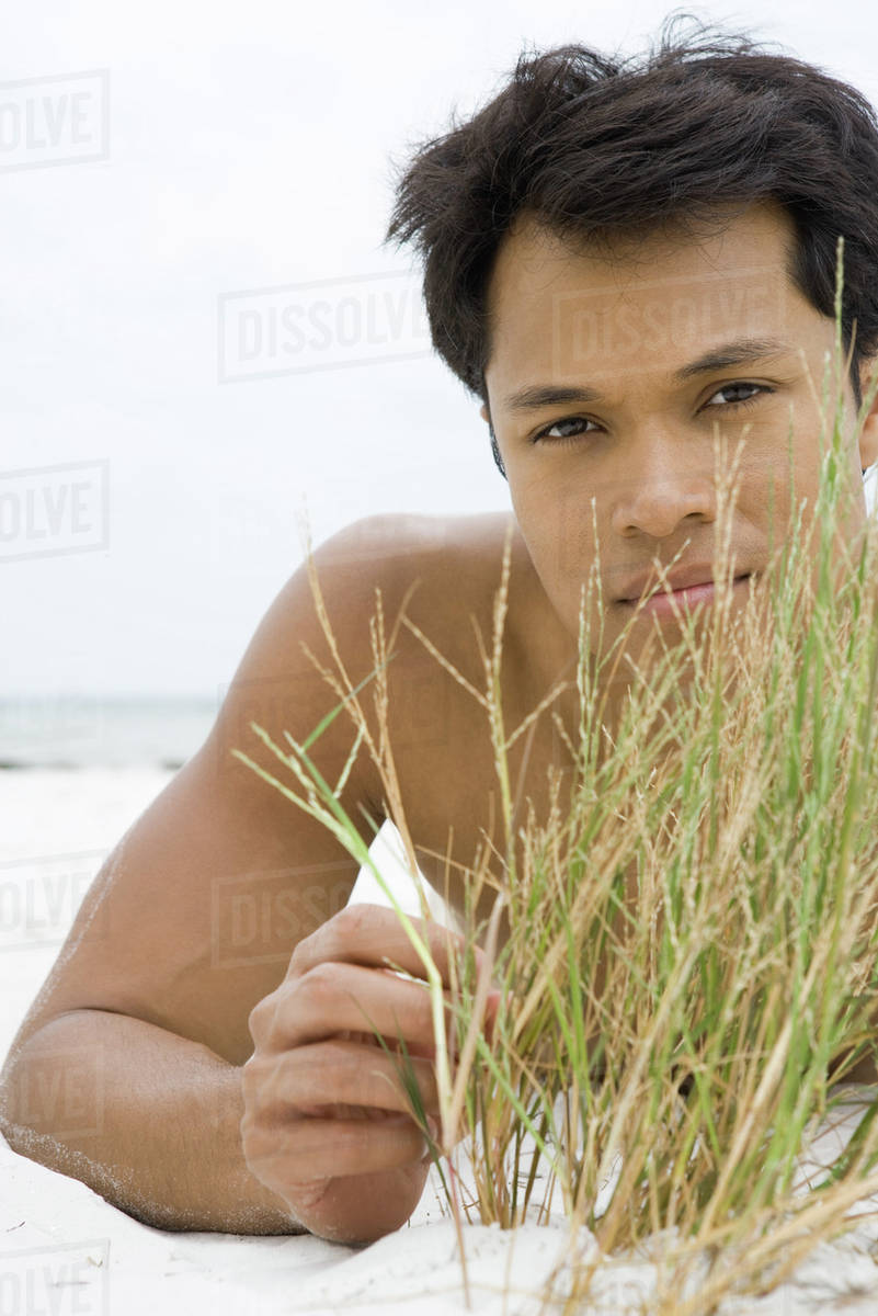 Man lying on the beach touching dune grass, looking at camera - Royalty ...
