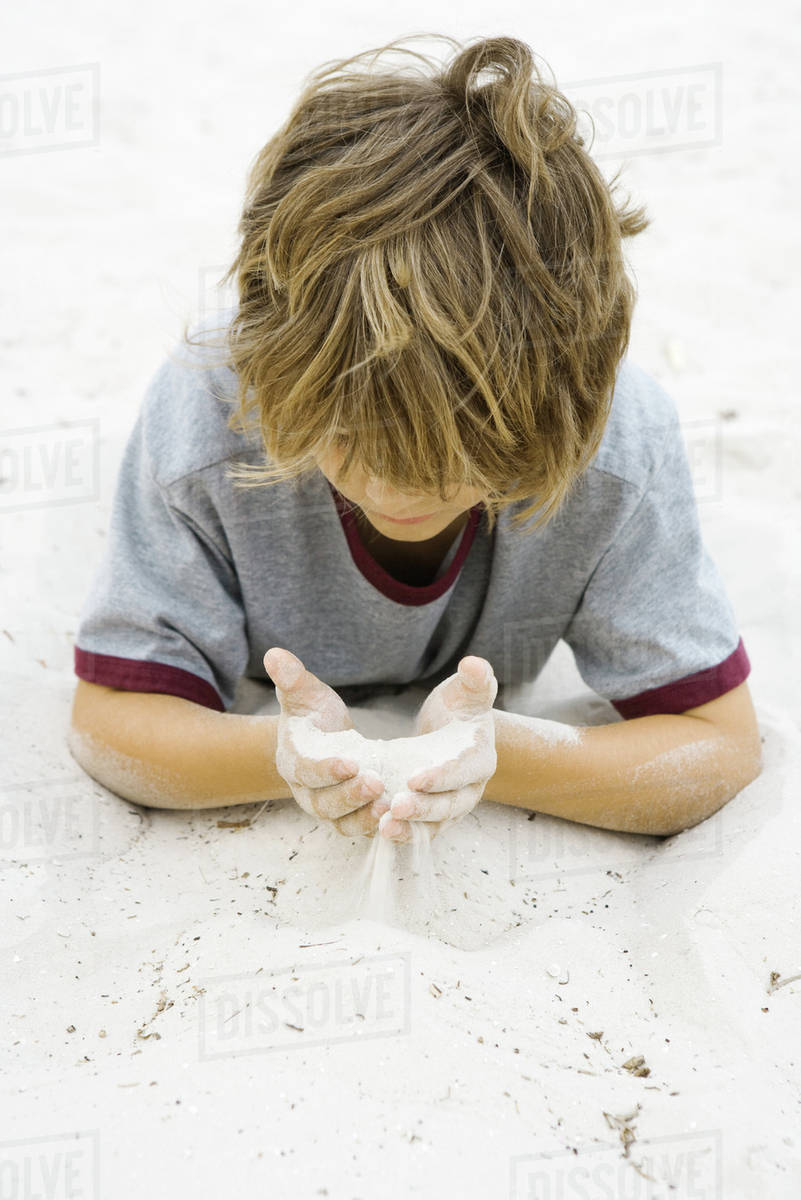 Boy lying on the ground, looking down at handful of sand - Stock Photo ...