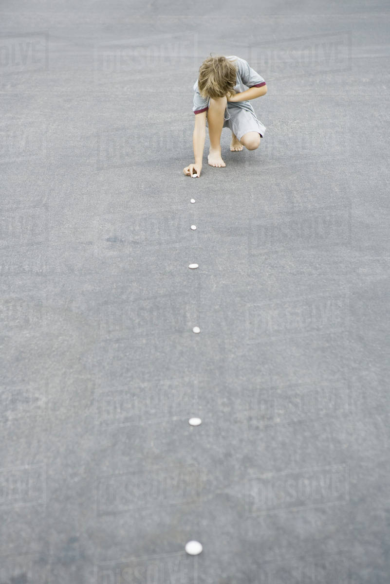 Child crouching on the ground, lining up pebbles, full length - Stock ...