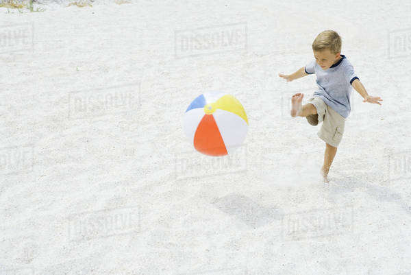 Young boy kicking beach ball at the beach, arms out - Royalty-free ...