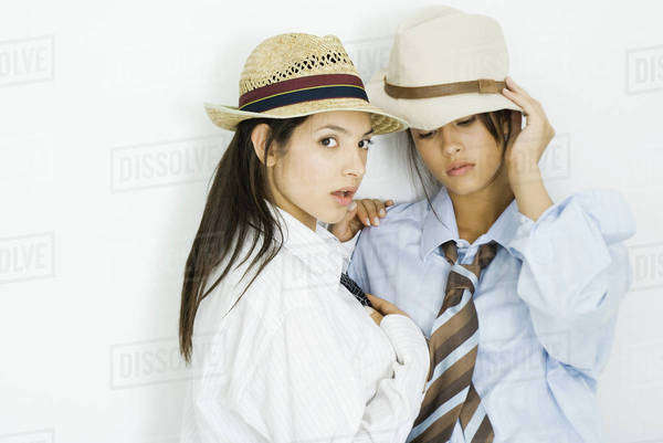 Two young females dressed in men's clothing and hats, one looking at ...