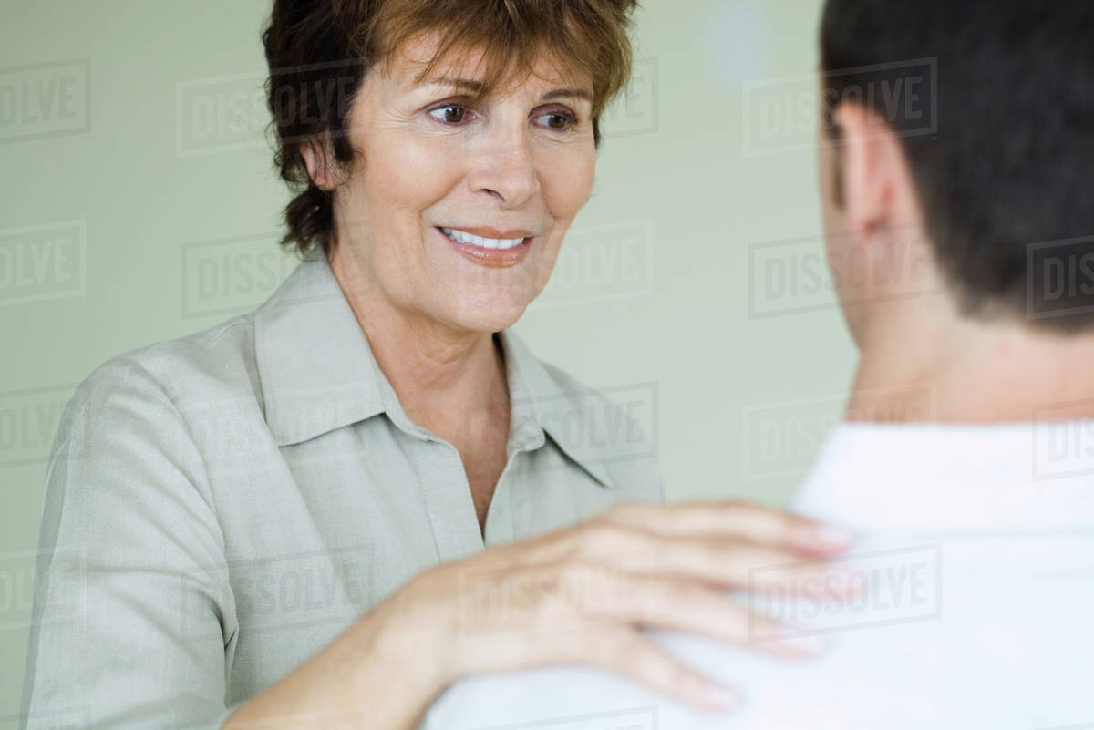Woman placing hand on adult son's shoulder, over the shoulder view ...