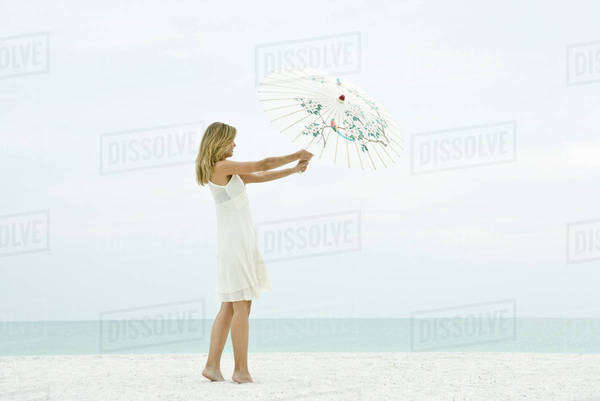 Woman holding parasol on beach, full length - Stock Photo - Dissolve