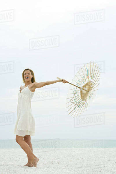 Woman holding parasol on beach, full length - Stock Photo - Dissolve