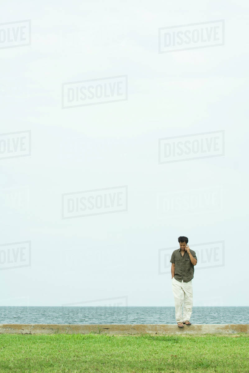 Man standing, using cell phone, body of water in background - Stock ...