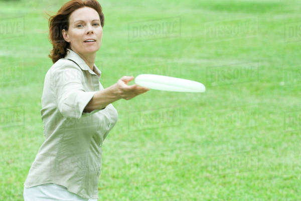 Woman throwing plastic disc, smiling at camera - Royalty-free Stock ...