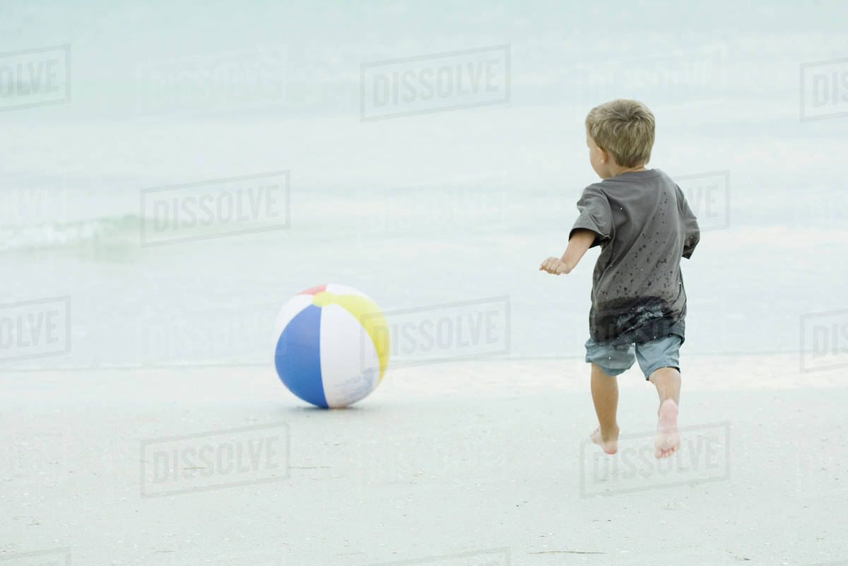Young boy running after beach ball at the beach, rear view - Royalty ...