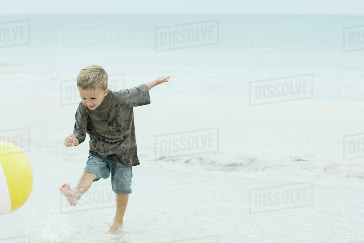 Little boy kicking beach ball at the beach - Stock Photo - Dissolve