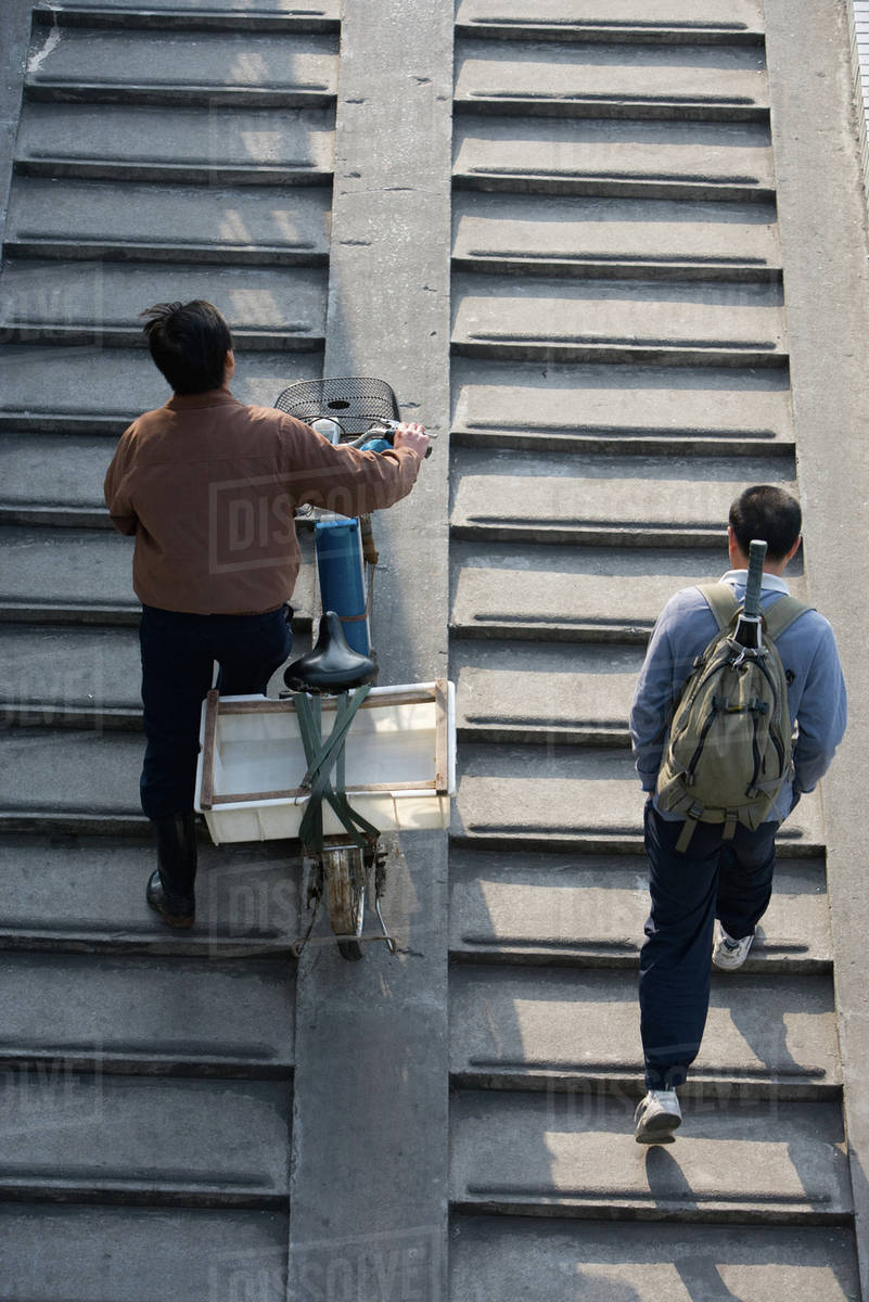 Pedestrians walking up steps, one pushing bicycle, viewed from directly ...