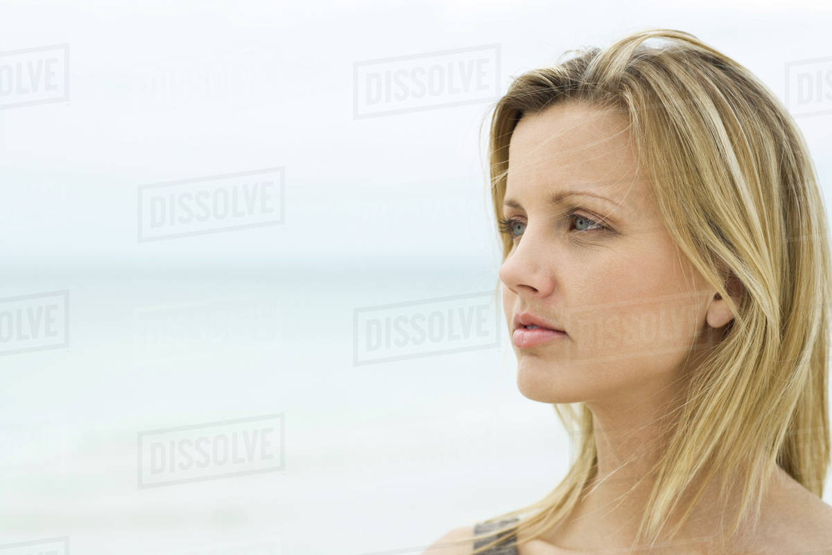 Blonde woman looking into distance, sea in background, head and ...