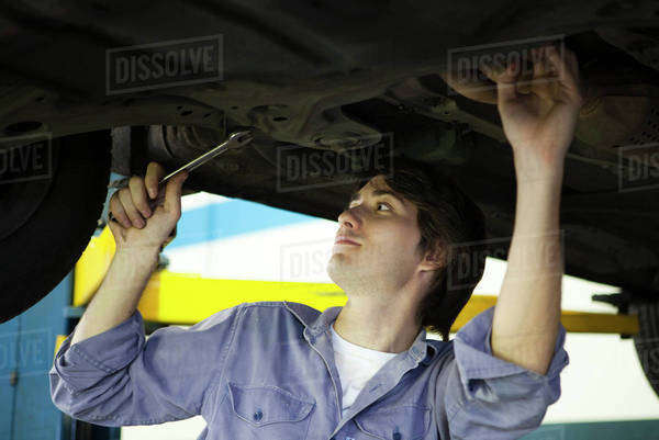 Mechanic working on underside of car elevated on hydraulic lift ...
