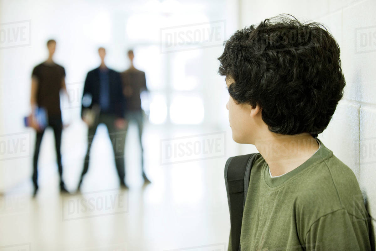 Teenage boy looking over shoulder at bullies in background - Stock ...