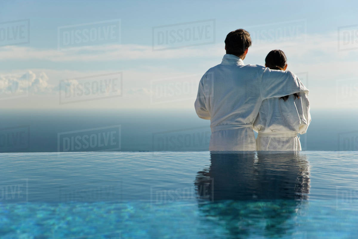 Couple standing at edge of infinity pool, looking at view - Stock Photo ...