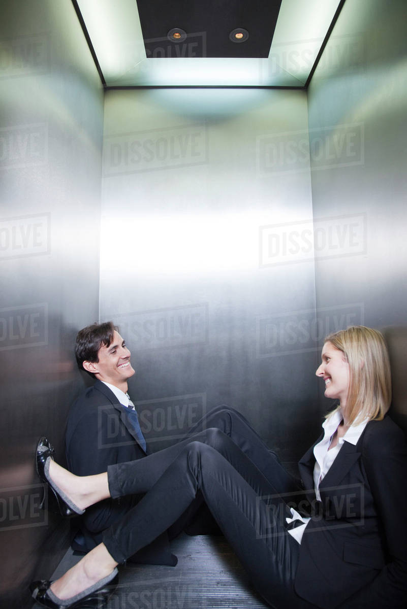 Professionals trapped in elevator, sitting on floor chatting - Royalty ...