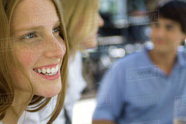Young woman smiling, friends in background - Stock Photo - Dissolve