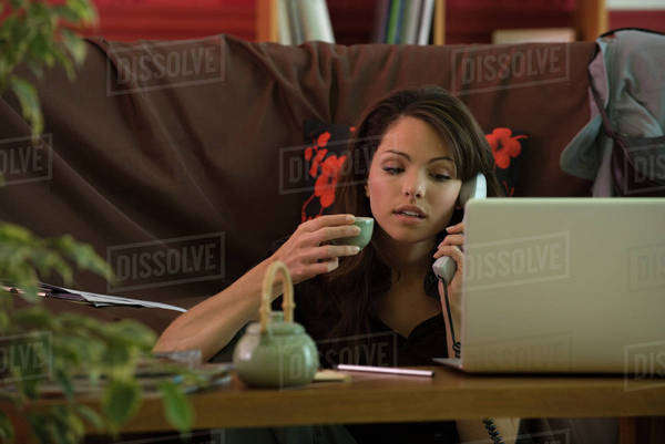 Young woman sitting at coffee table using phone and laptop computer ...
