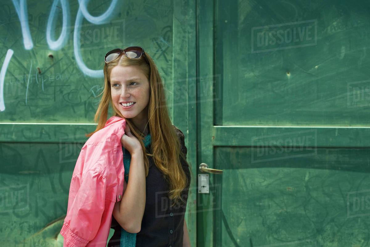 Fashionable young woman standing in front of graffitied door, jacket ...