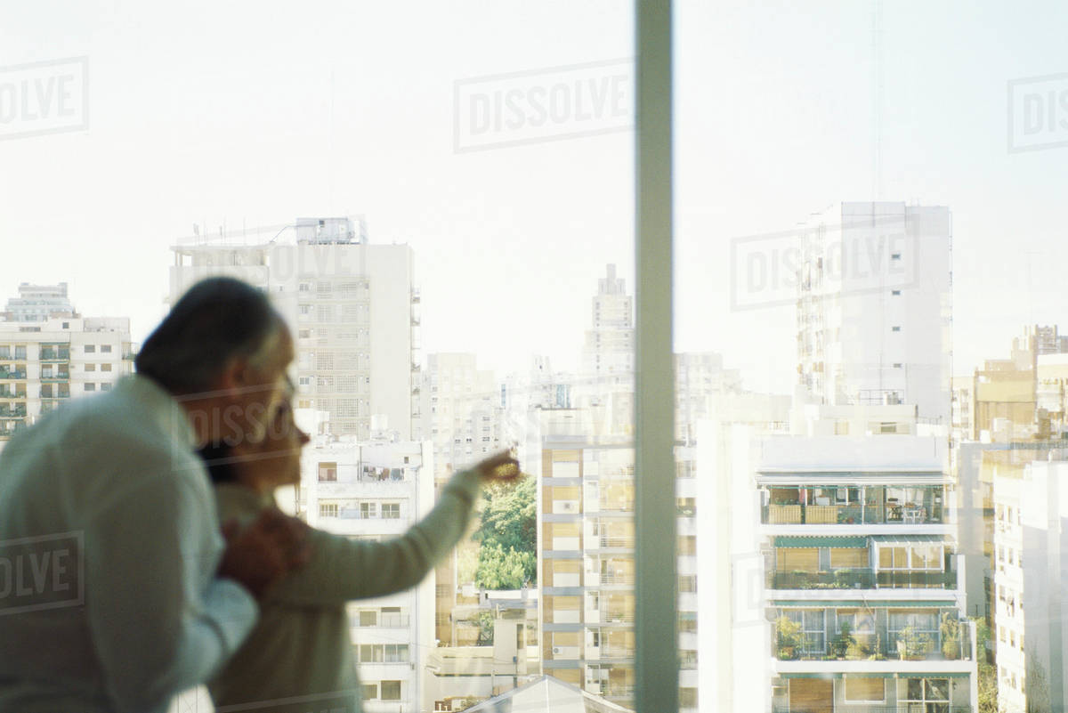 Mature couple looking out view at view of city skyline, woman pointing ...