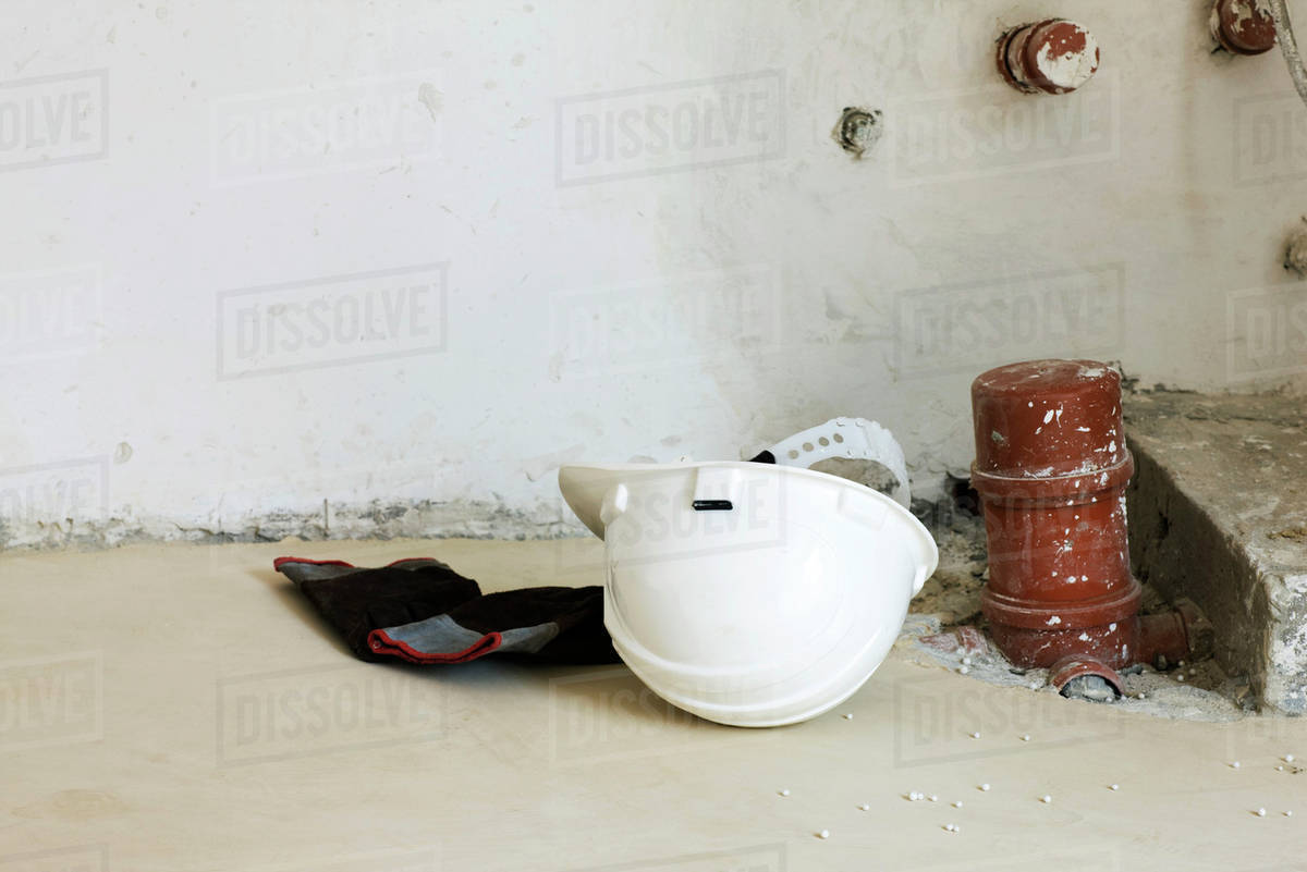 Gloves, hard hat on floor near plumbing fixture - Stock Photo - Dissolve