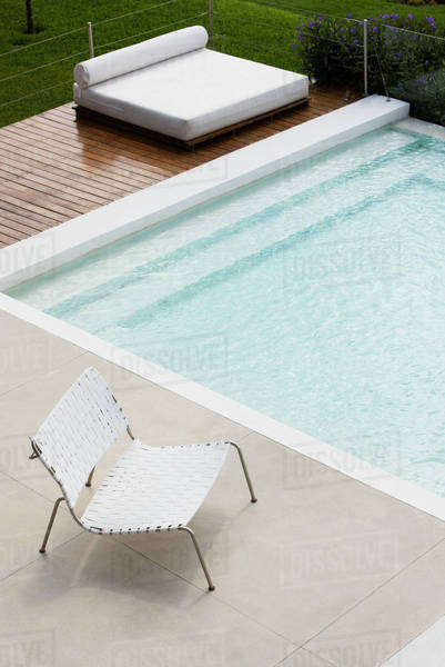 Chair at edge of pool, sunbathing bed on deck in background - Stock ...